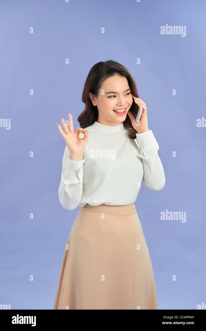 Young woman talking mobile over isolated purple background showing ok ...