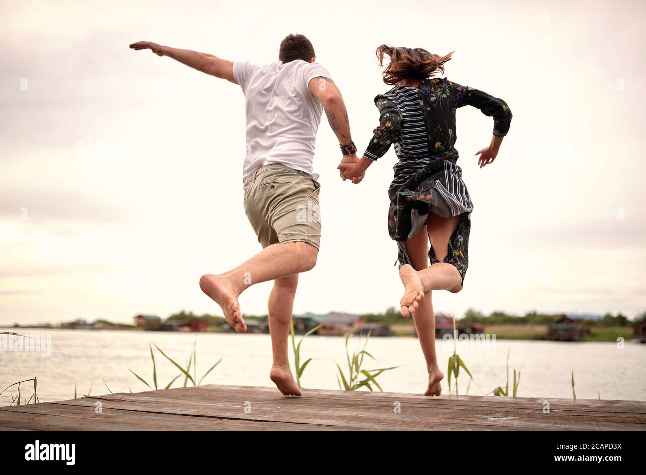 young caucasian adult couple jumping together in the river holding ...
