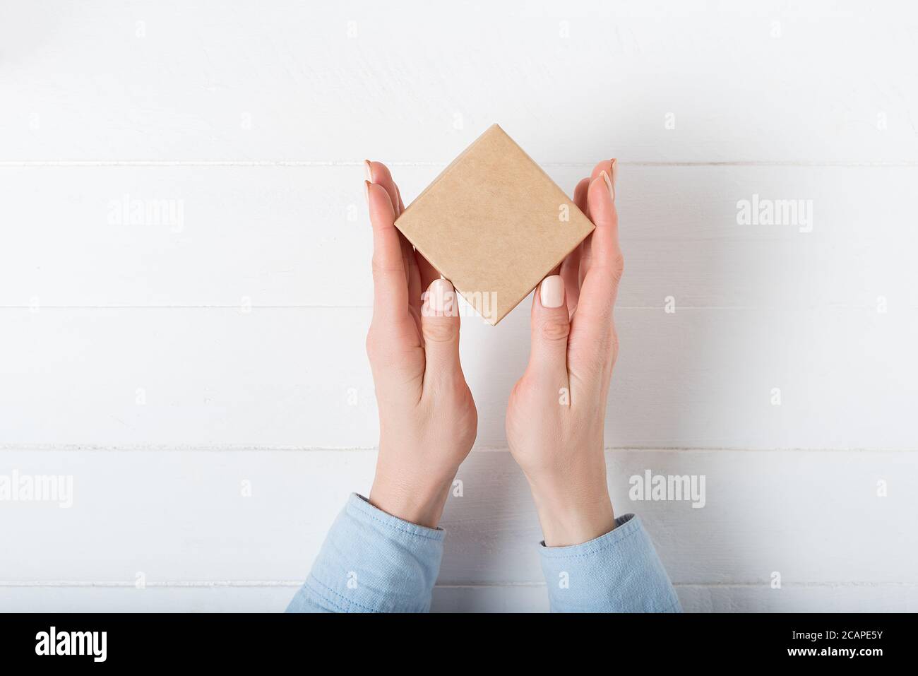 Small square cardboard box in female hands. Top view, white background ...