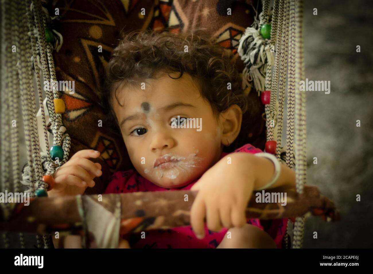 a North Indian baby child eating curd at home with his face on black ...