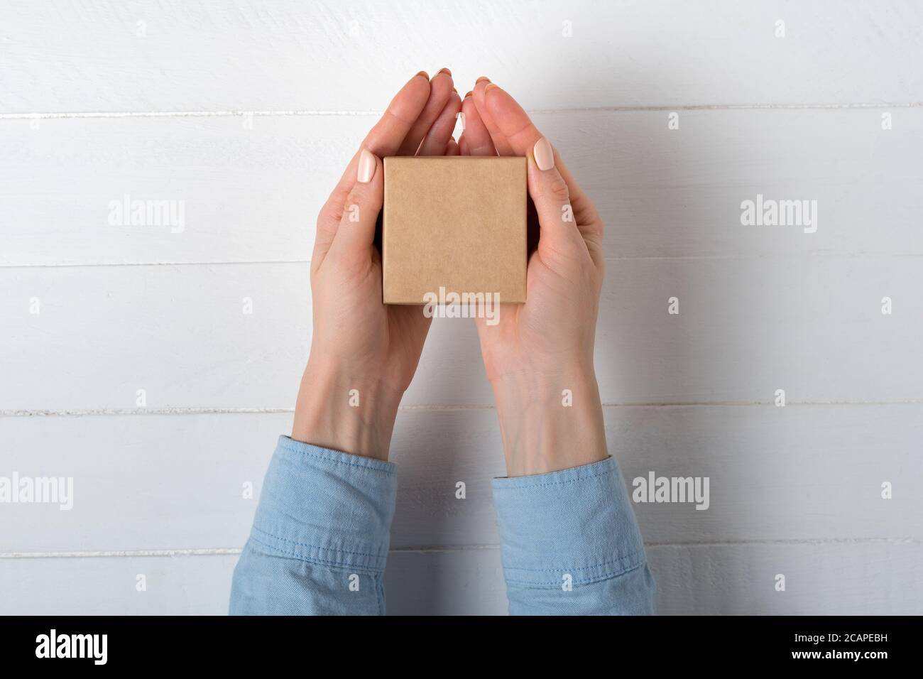 Small square cardboard box in female hands. Top view, white background ...