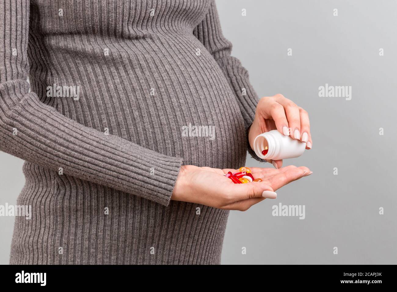 Close up of pregnant woman taking a pile of pills from a bottle at ...