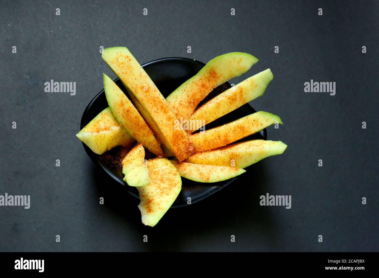 Fresh green mango with mixed salt and ground chilli powder over black ...