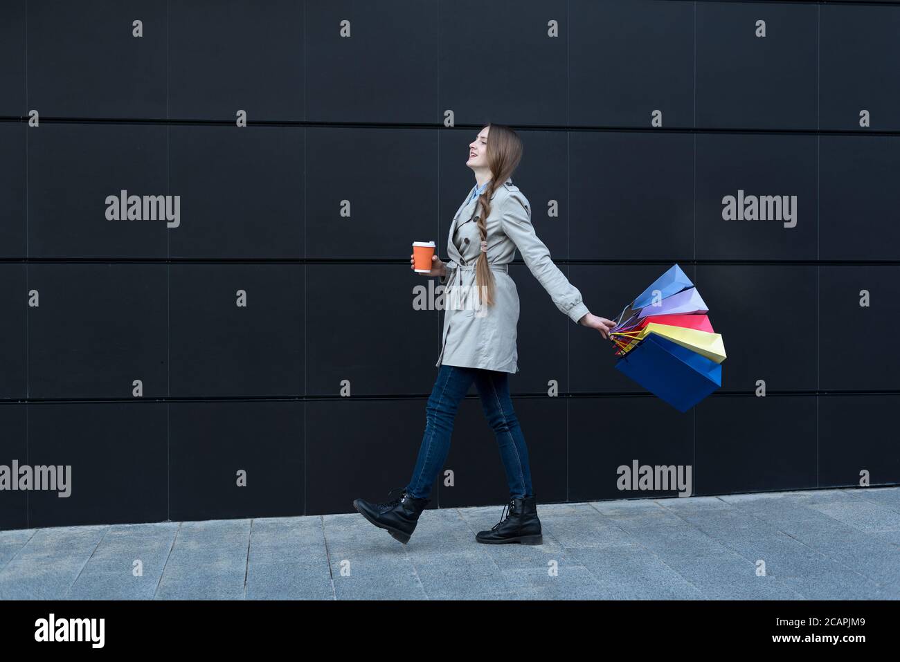 Happy young woman with colorful bags and paper cup walking on the ...