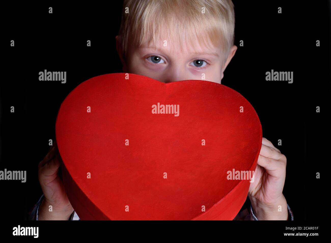 Embarrassed blond boy holding a red box in the shape of a heart on ...