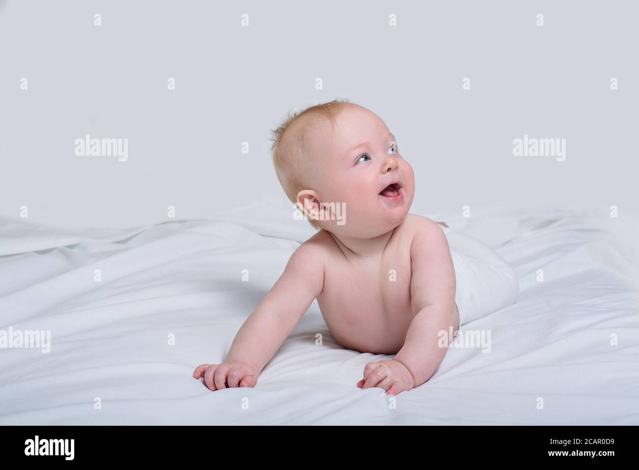 Smiling baby on his tummy. Looking up with surprised expression. White ...