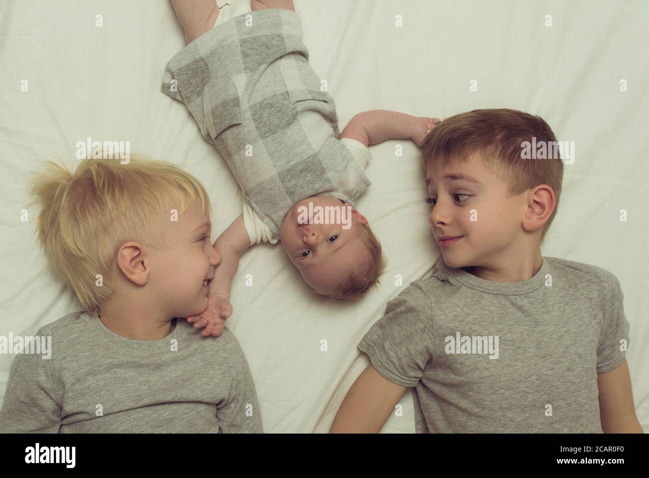 Two older brothers and youngest baby in a white bed. Happy childhood ...