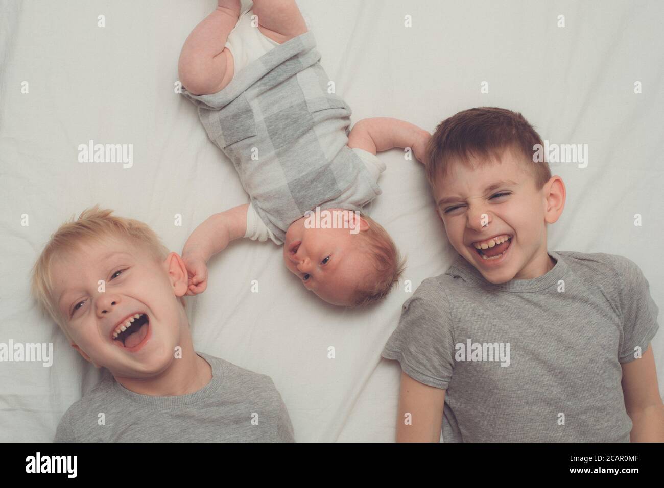 Two older brothers and youngest baby in a white bed. Happy childhood ...