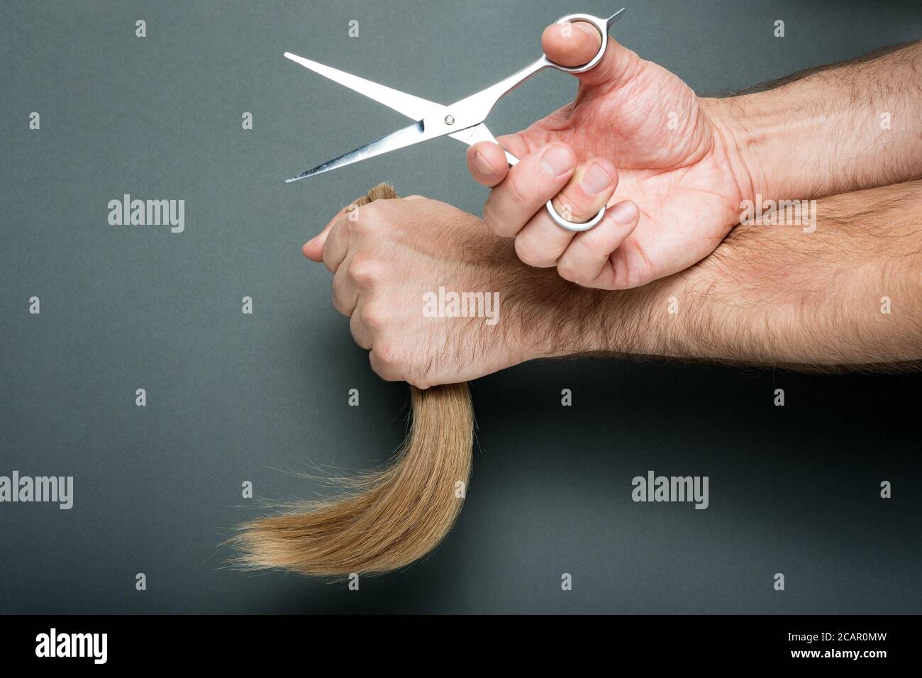Men's hands demonstrate scissors and cut hair on a dark background ...