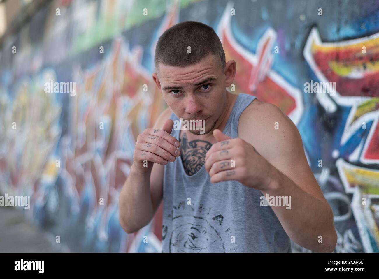 A bully guy in a sports shirt near a wall with graffiti Stock Photo - Alamy