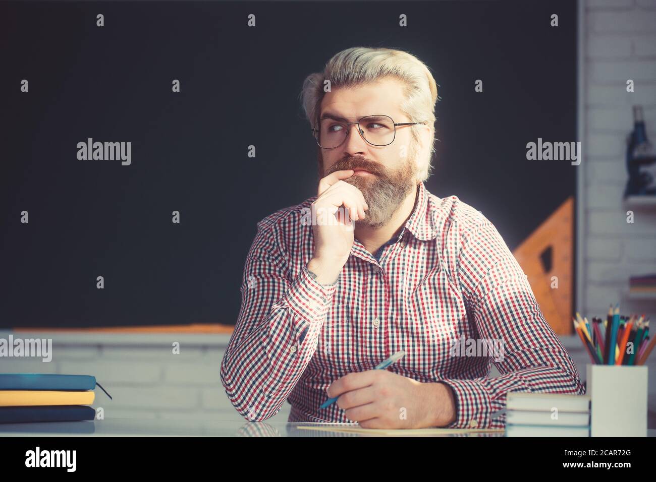 Attractive male teacher sitting thinking at his desk with his hand ...