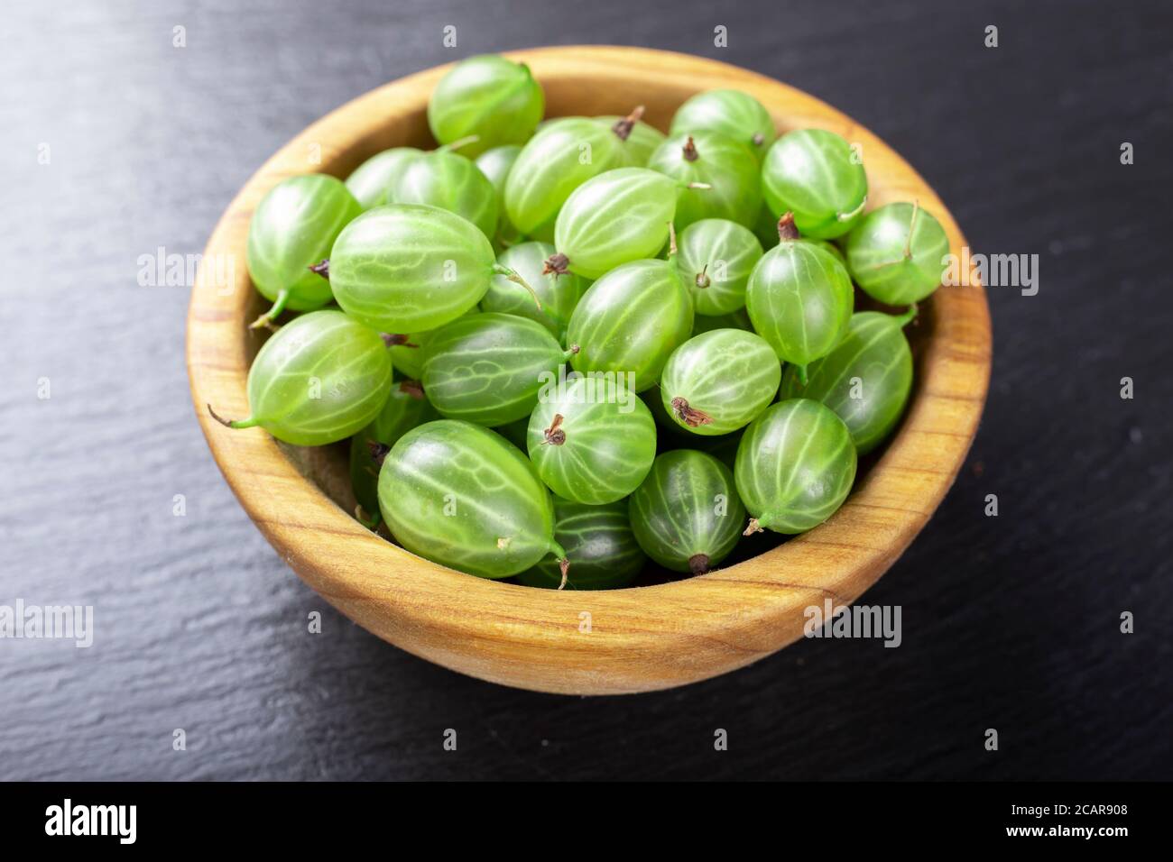 Fresh gooseberries in wooden bowl on black stone slate background. Top ...