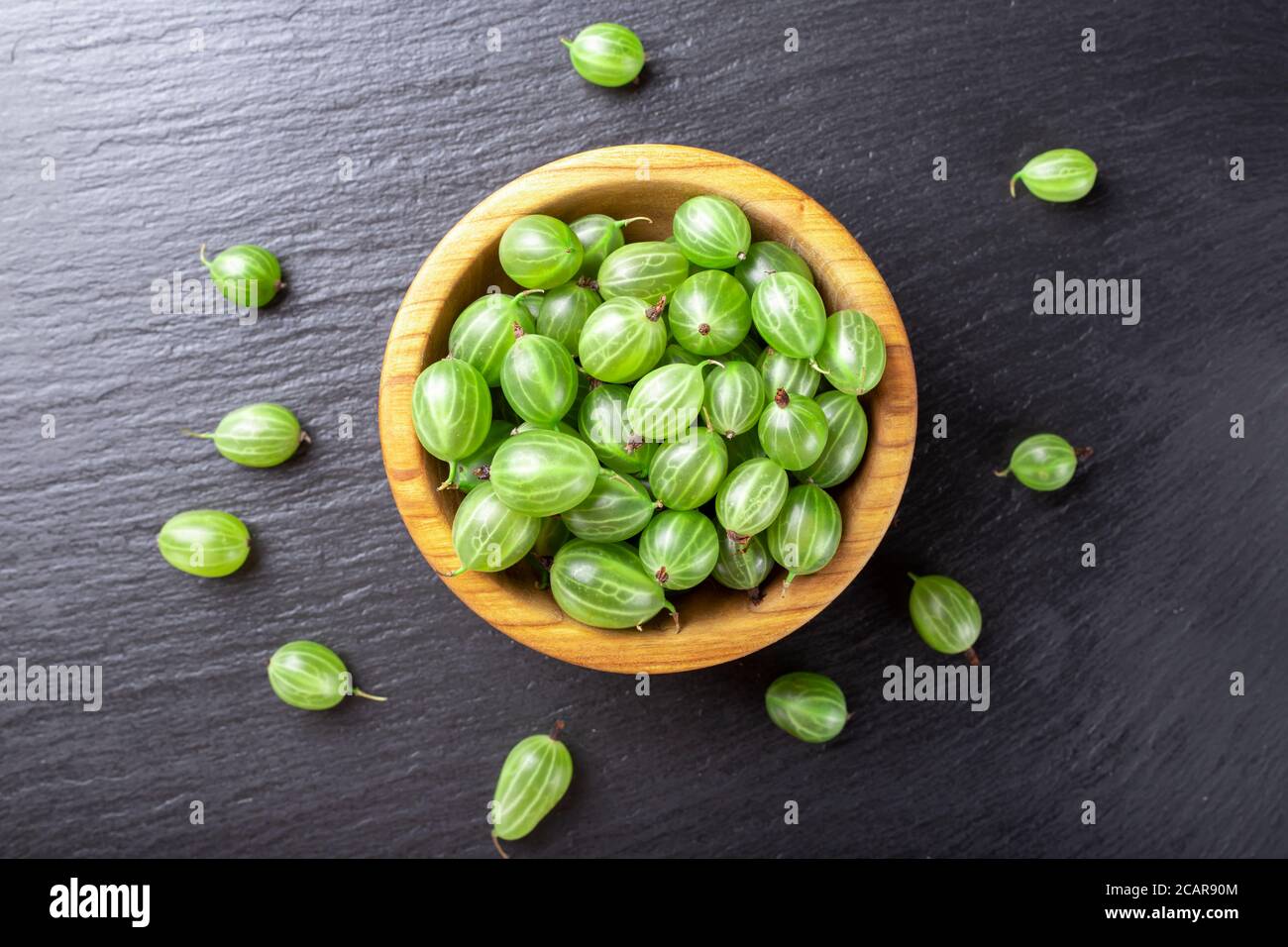 Fresh gooseberries in wooden bowl on black stone slate background. Top ...