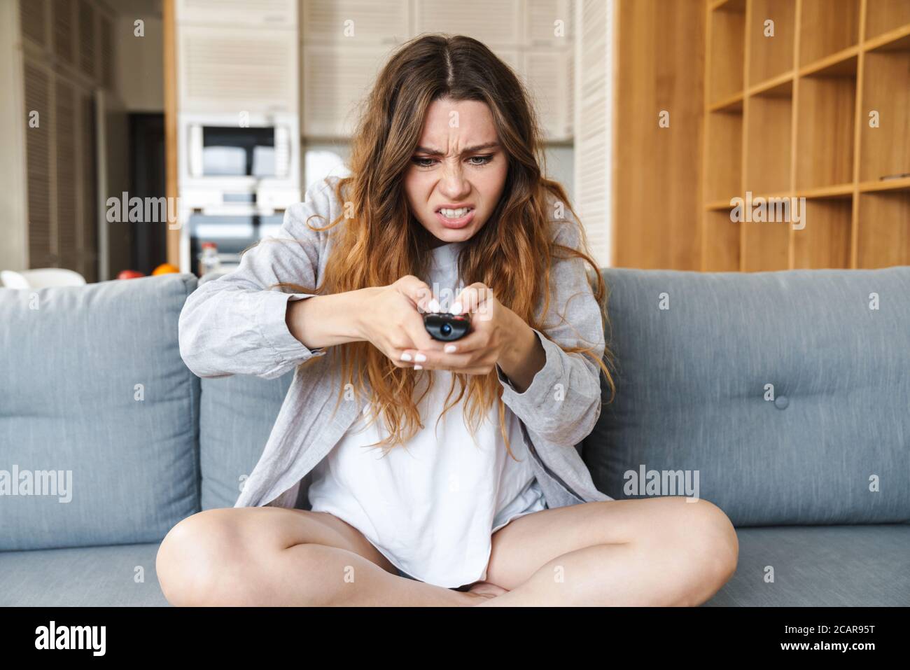 Angry young woman relaxing on a couch at home, holding tv remote ...