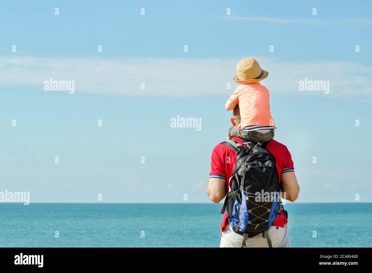 Father and son on their shoulders stand on the sea shore, rear view ...