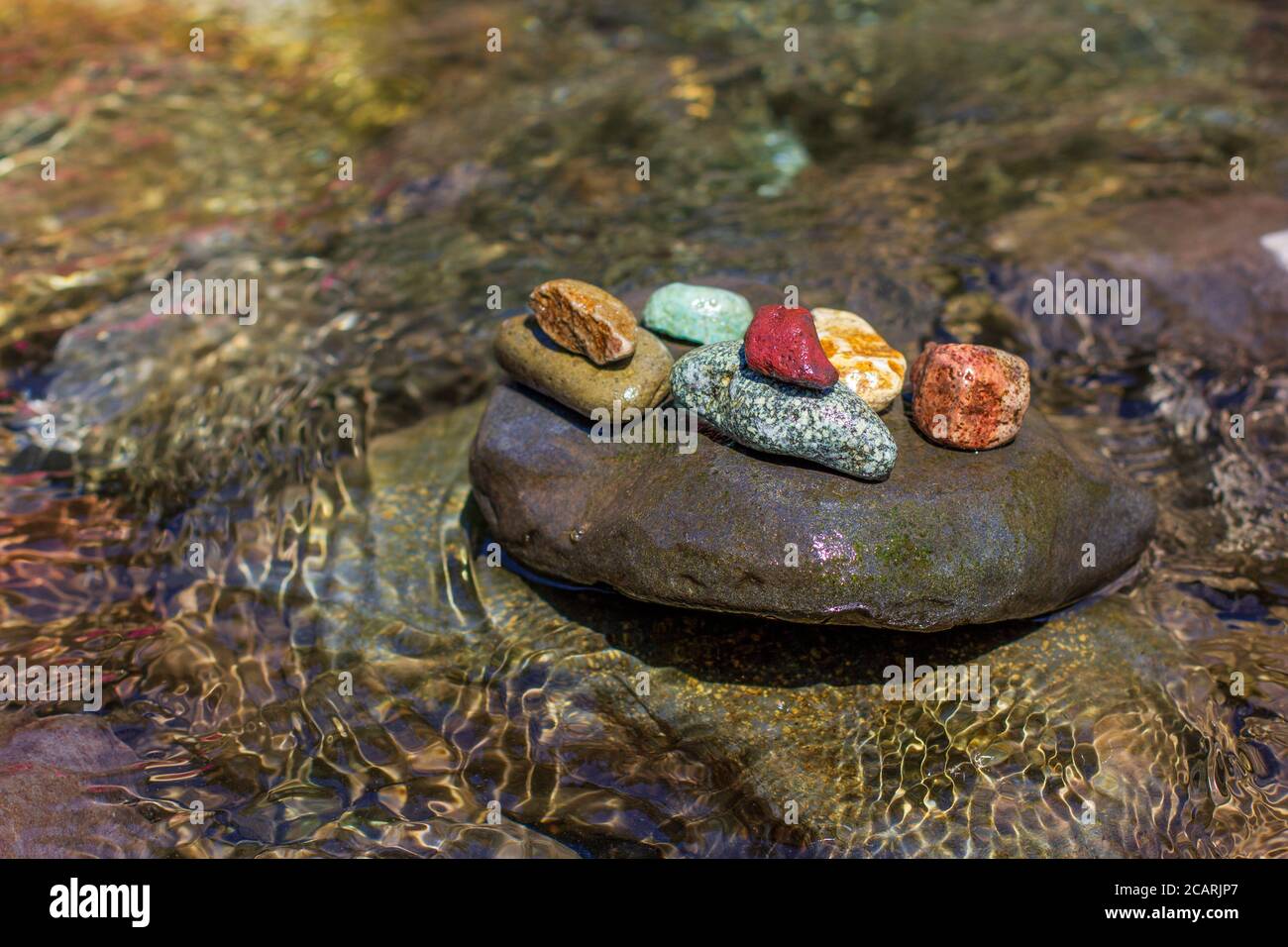 Collection of colorful wet river rocks sits on top of a larer rock in a ...