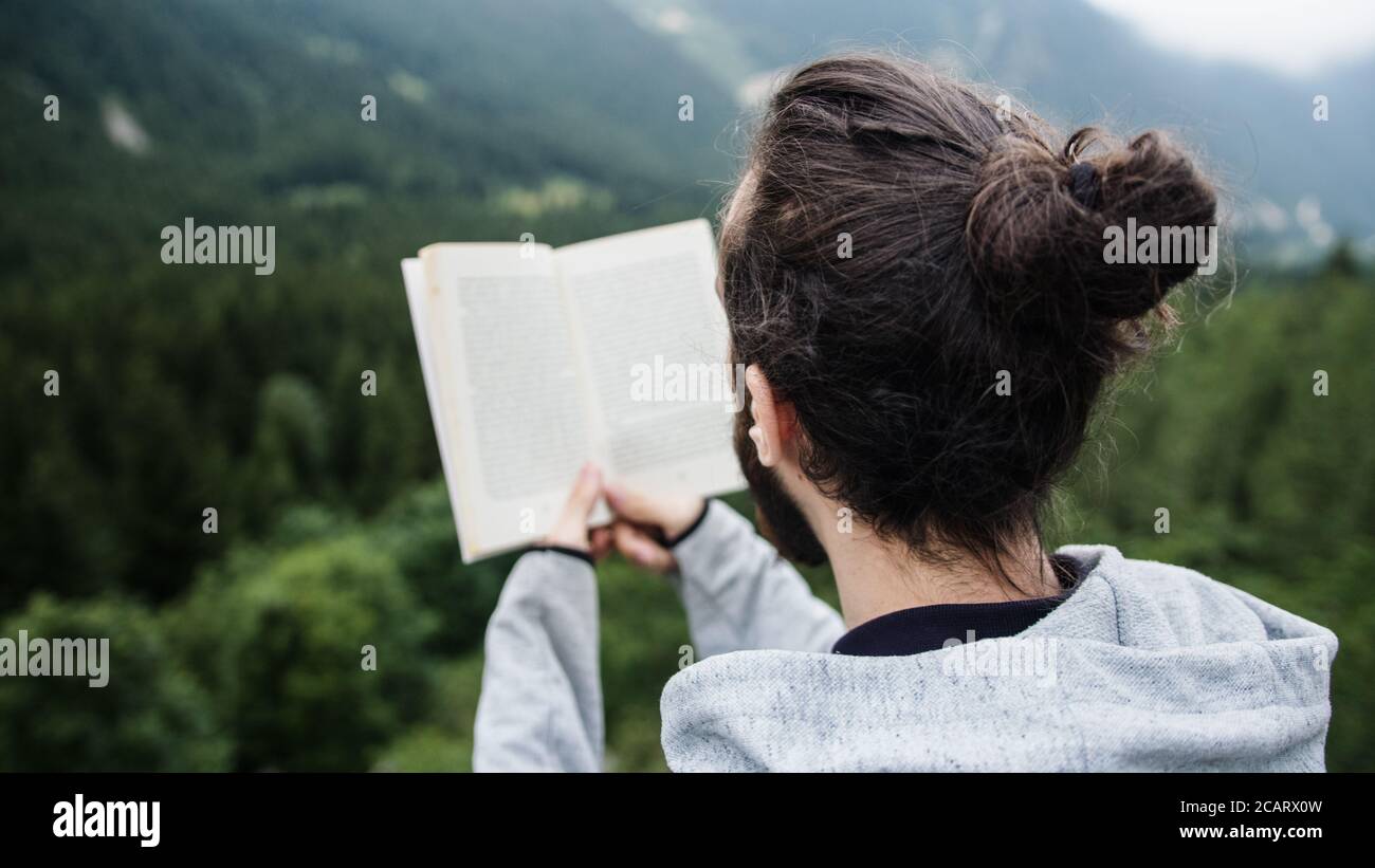 Man is reading a book at the landscape with pine trees in the forest ...