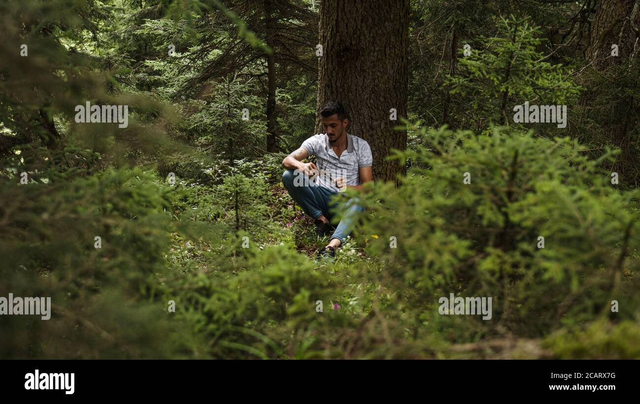 Handsome young man leaning on tree is dealing with wood stick in his ...