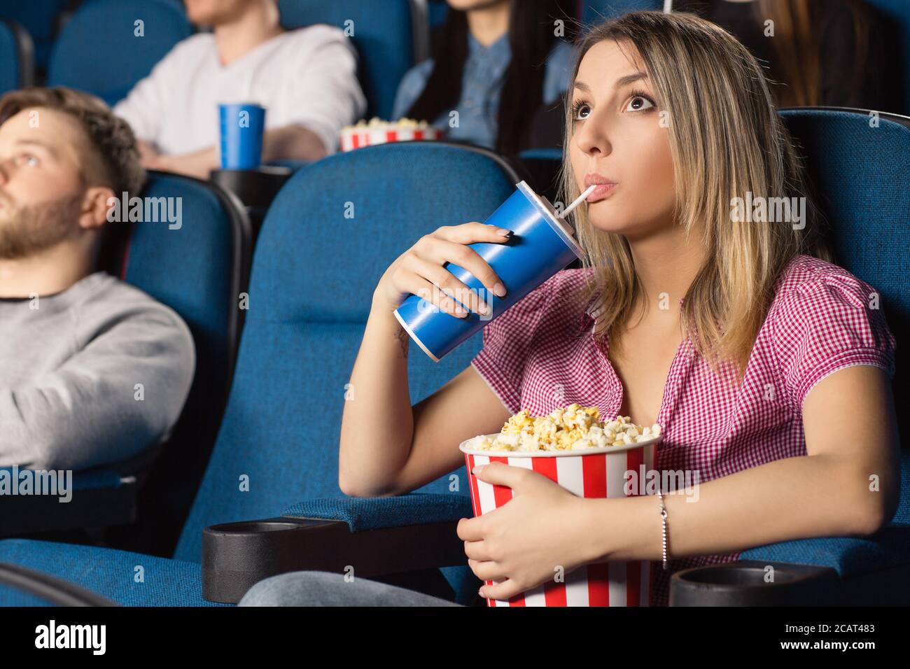 Movie night. Beautiful young female drinking and eating popcorn ...