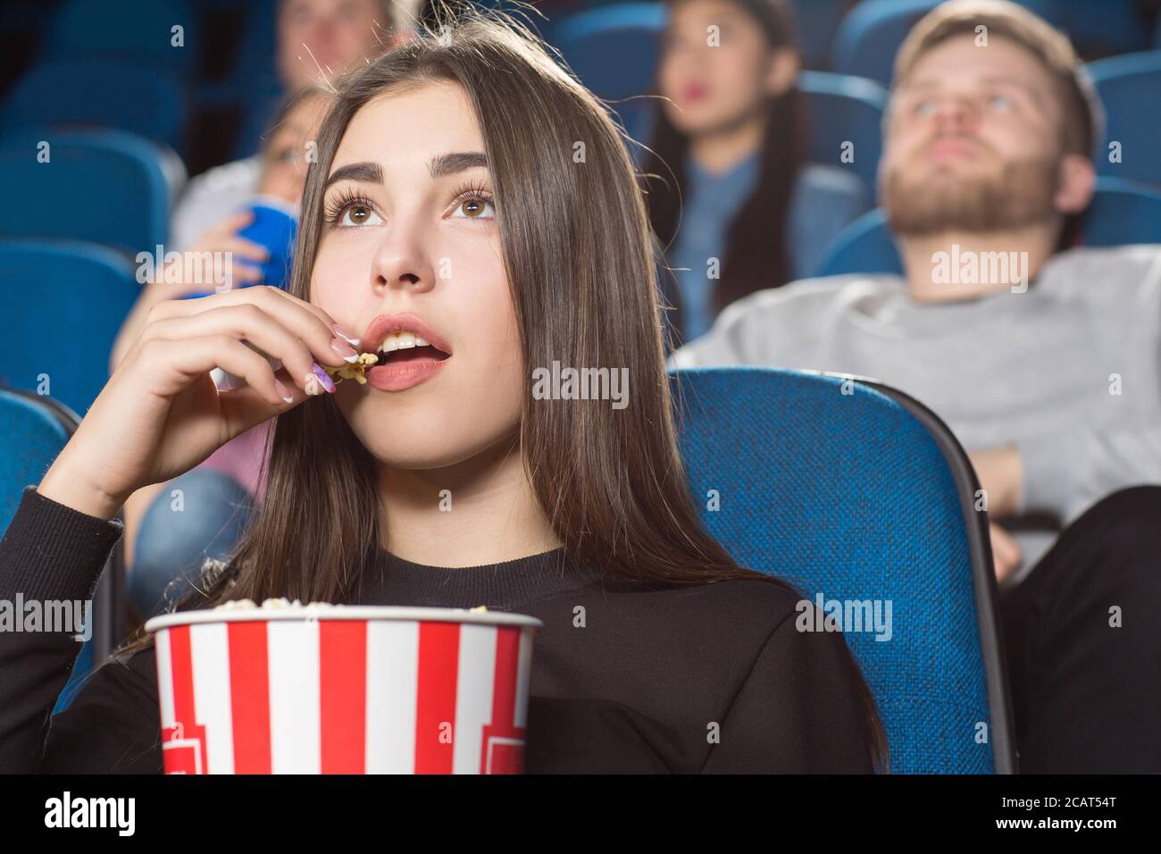 Perfect movie snack. Attractive brunette female eating popcorn while ...