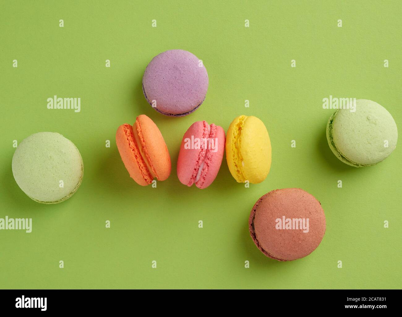 baked multi-colored macaroon cookies lie in a row on a green background ...