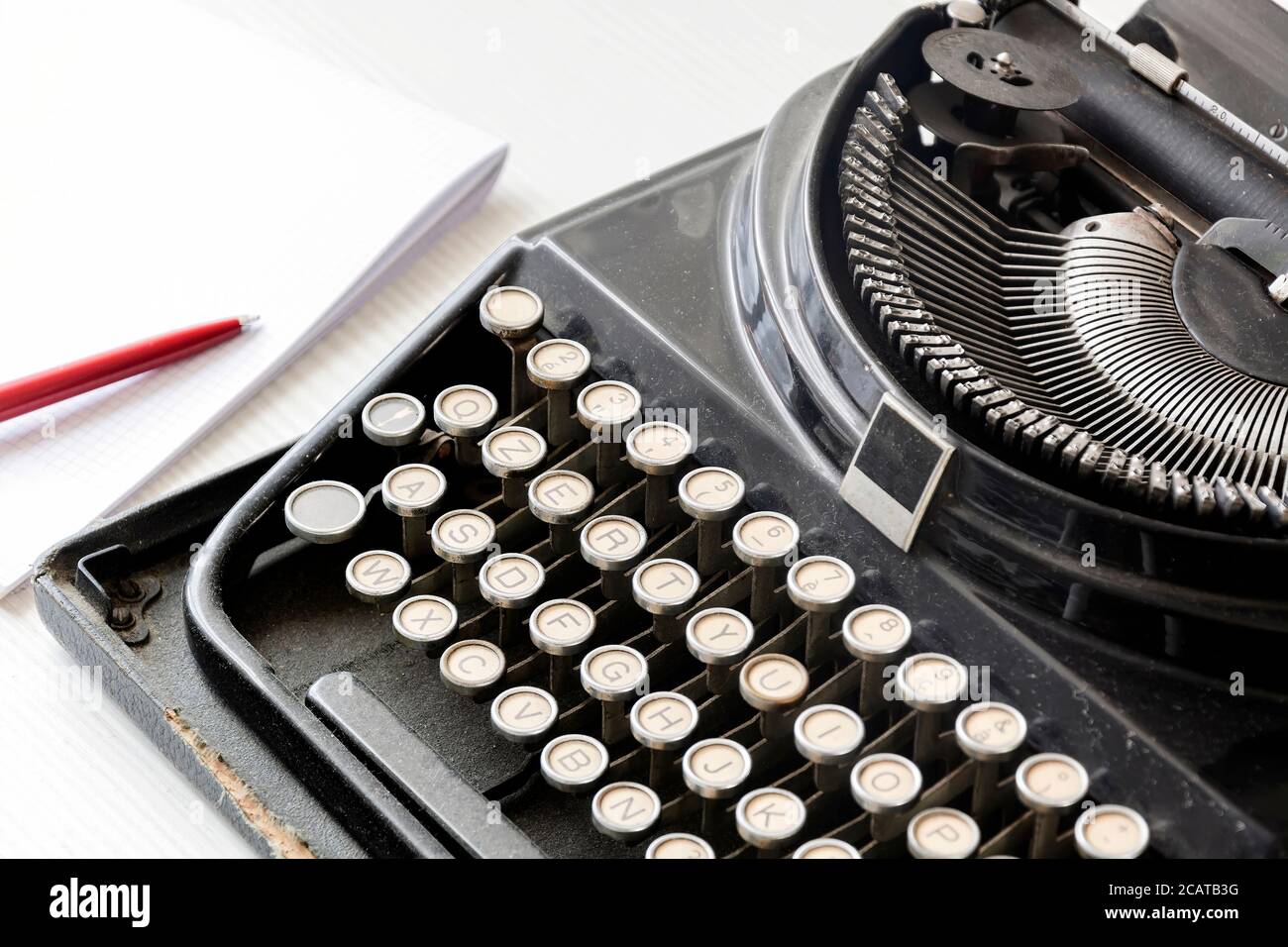an old black typewriter next to a white sheet of paper with a red pen ...