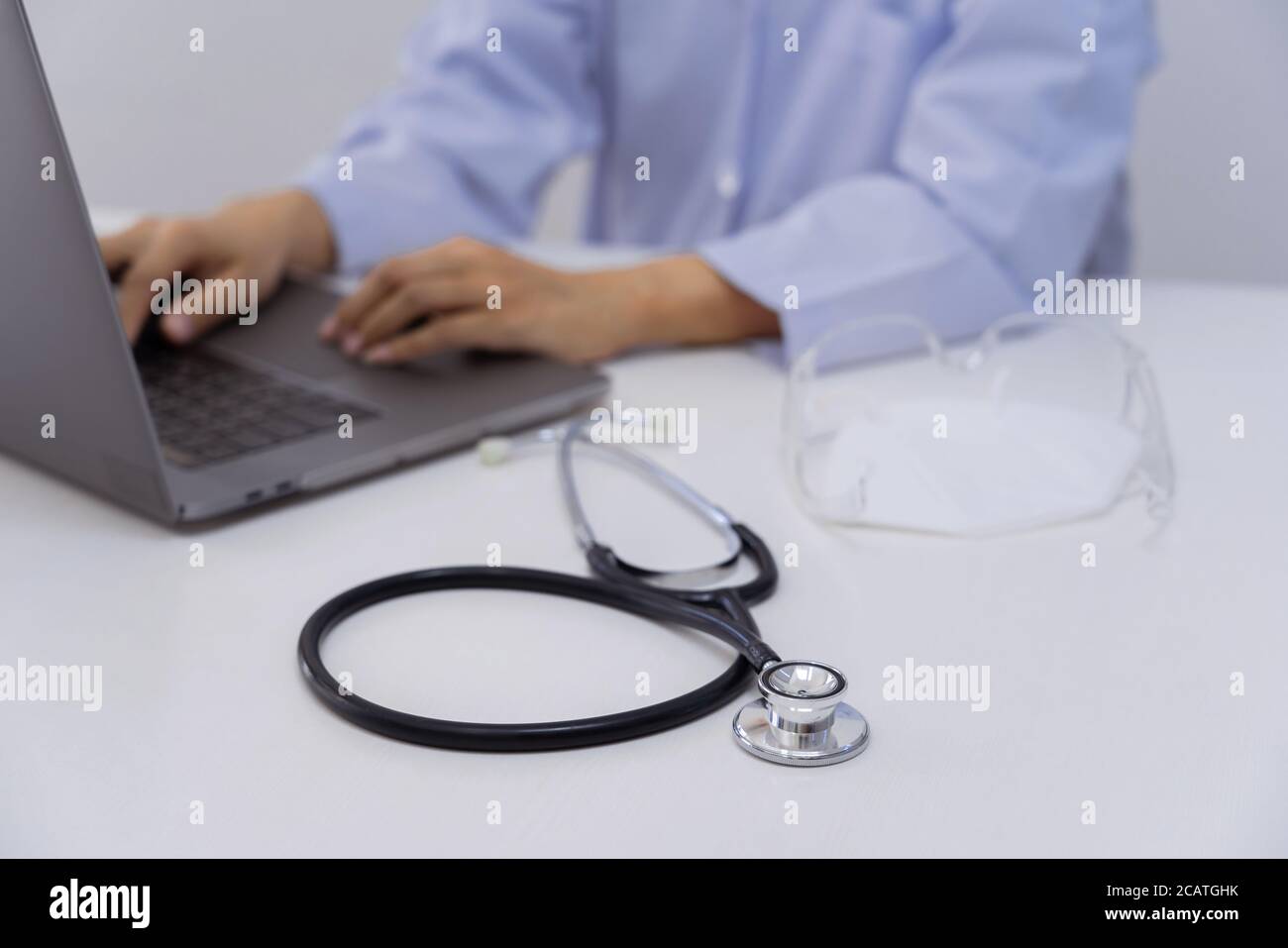 doctor working with laptop computer sitting at desk in hospital office ...