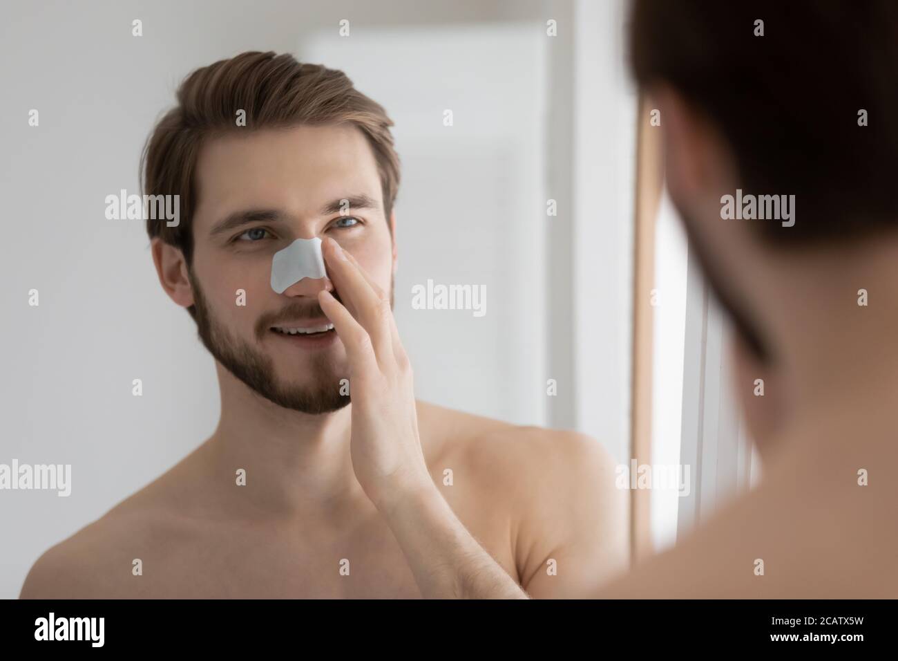 Mirror reflection smiling man applying anti blackhead mask on nose ...