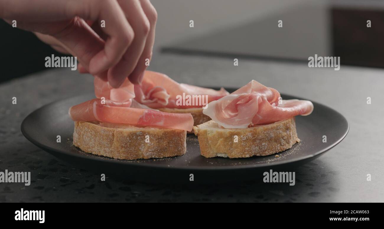 man hand put prosciutto on ciabatta slices black plate Stock Photo - Alamy