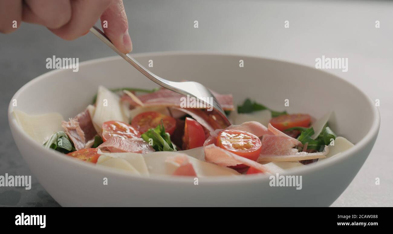 man hand pick salad with arugula, prosciutto and cherry tomatoes in ...