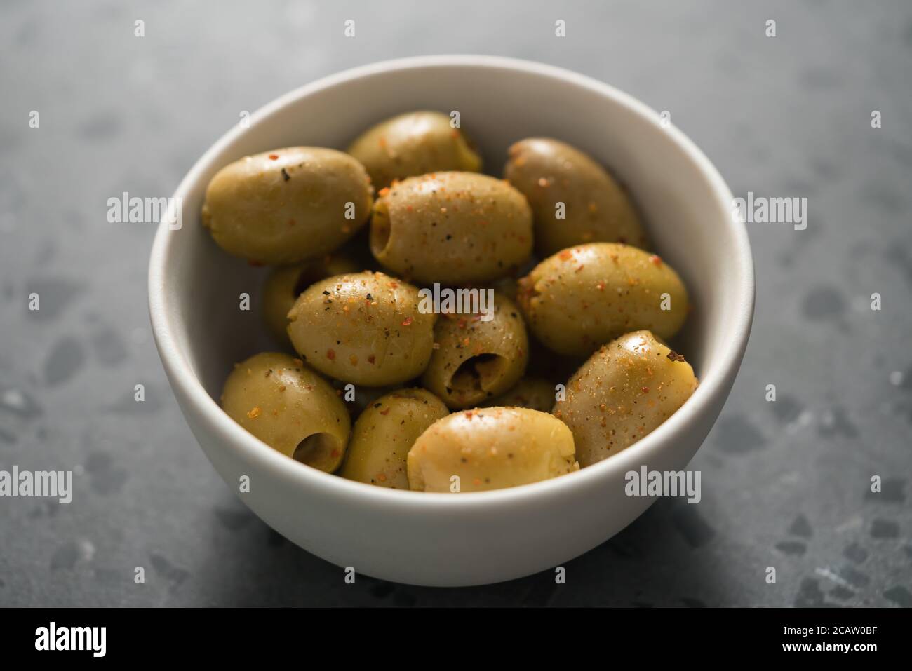 Closeup pitted whole green olives with spices in white bowl on terrazzo ...