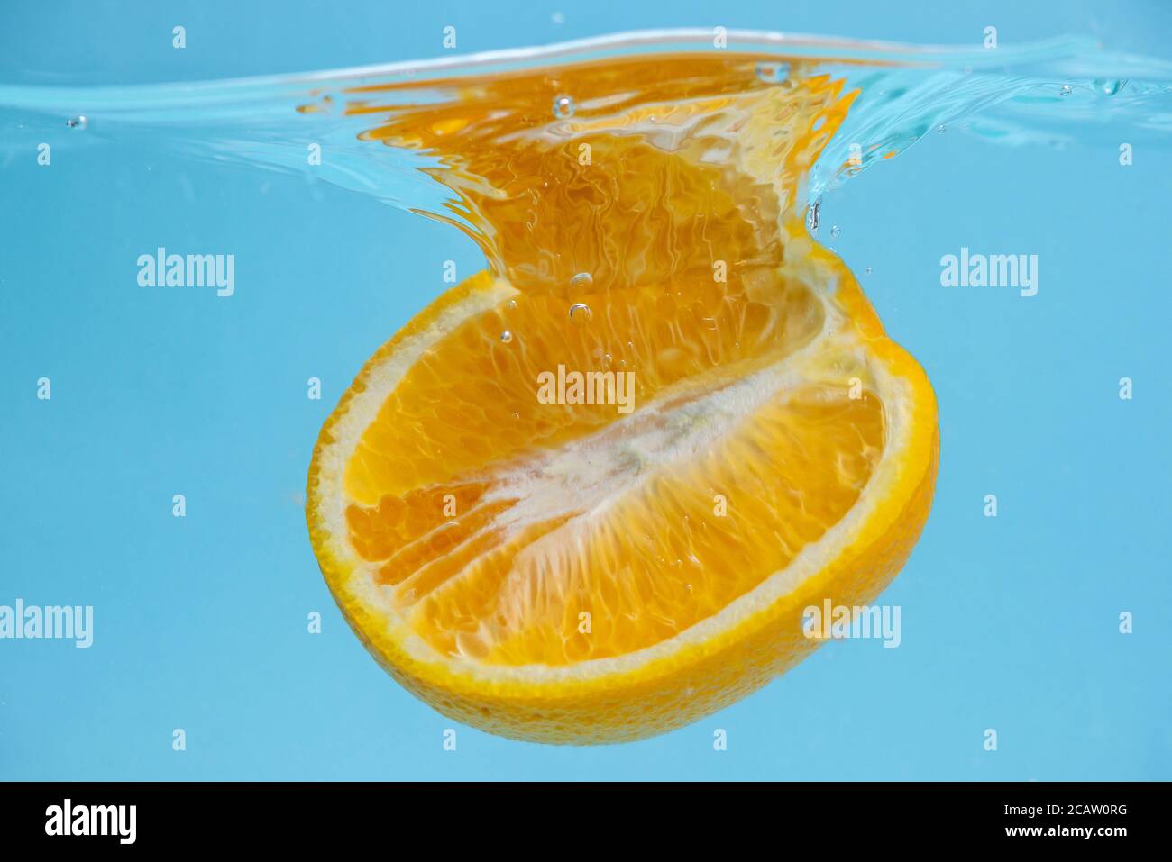 Half of a appetizing ripe orange is falling into the clear water ...