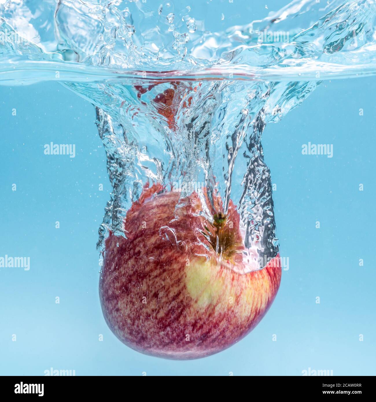 Ripe red apple is falling into clear water, forming lots of splashes ...