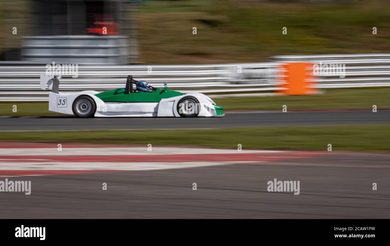 A panning shot of a white and green racing car as it circuits a track ...