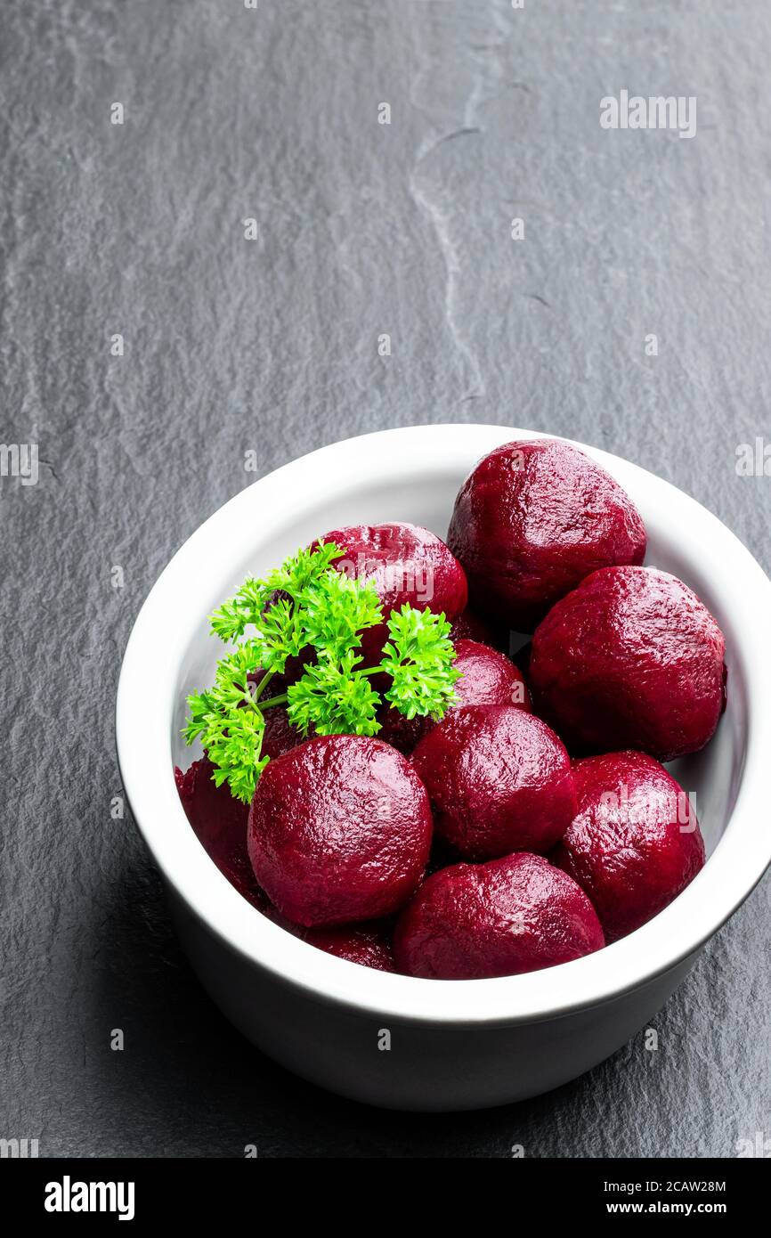 Homemade pickled baby beetroot in clay pot on black stone background ...