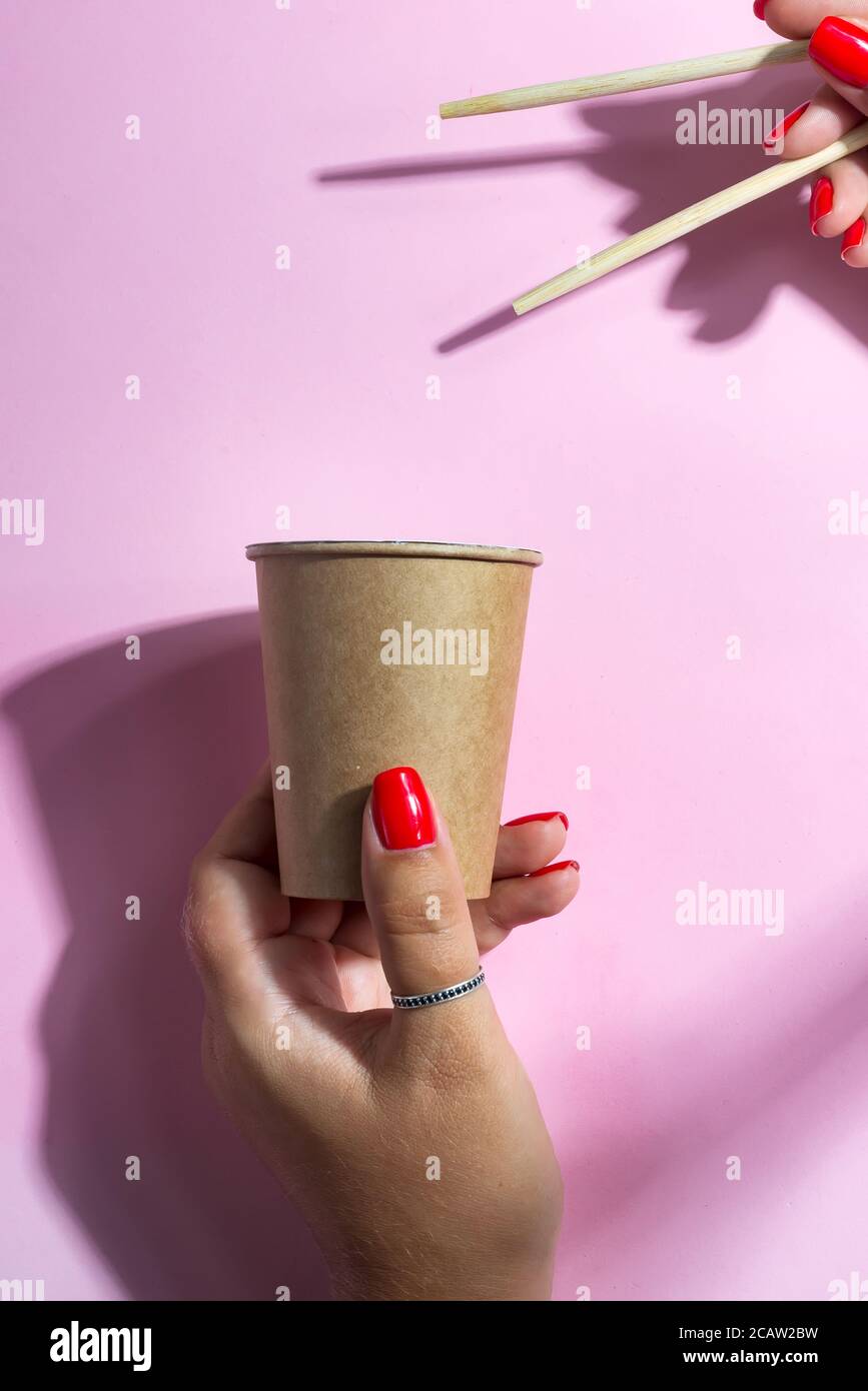 Woman's hands hold paper cup and wooden sticks above pastel pink ...