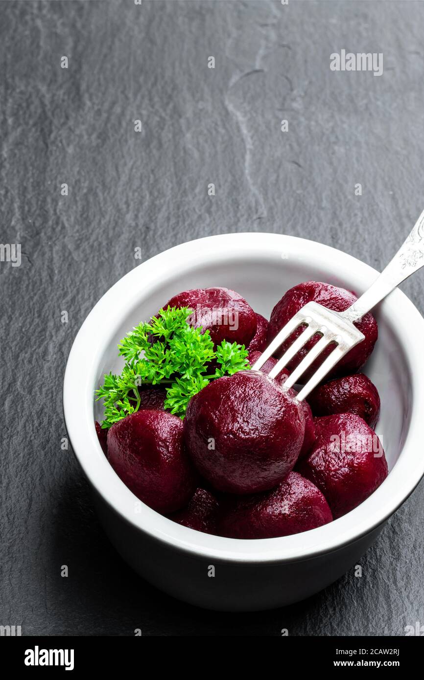 Homemade pickled baby beetroot in clay pot on black stone background ...