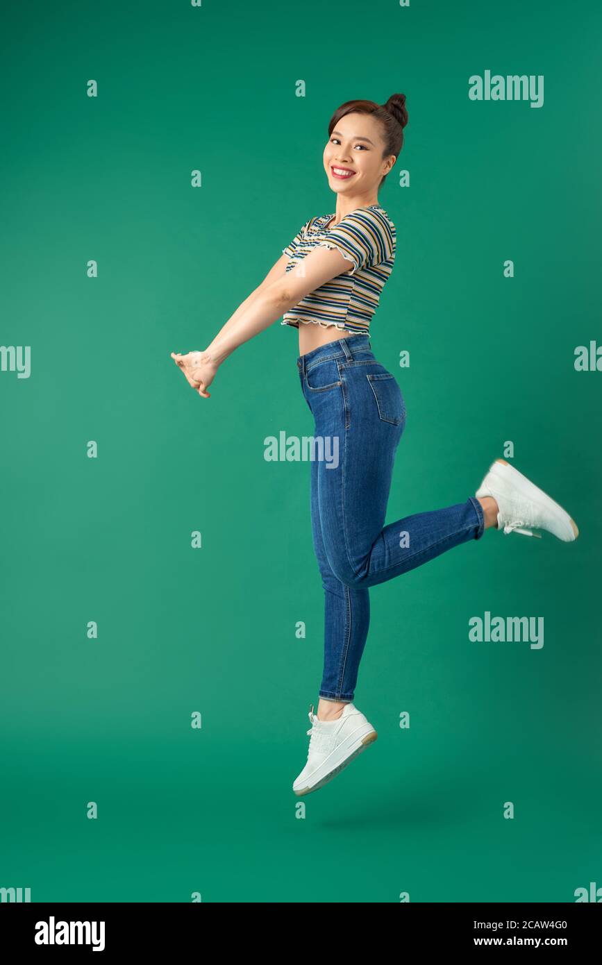 Full length of portrait of joyful young Asian woman jumping in air over ...