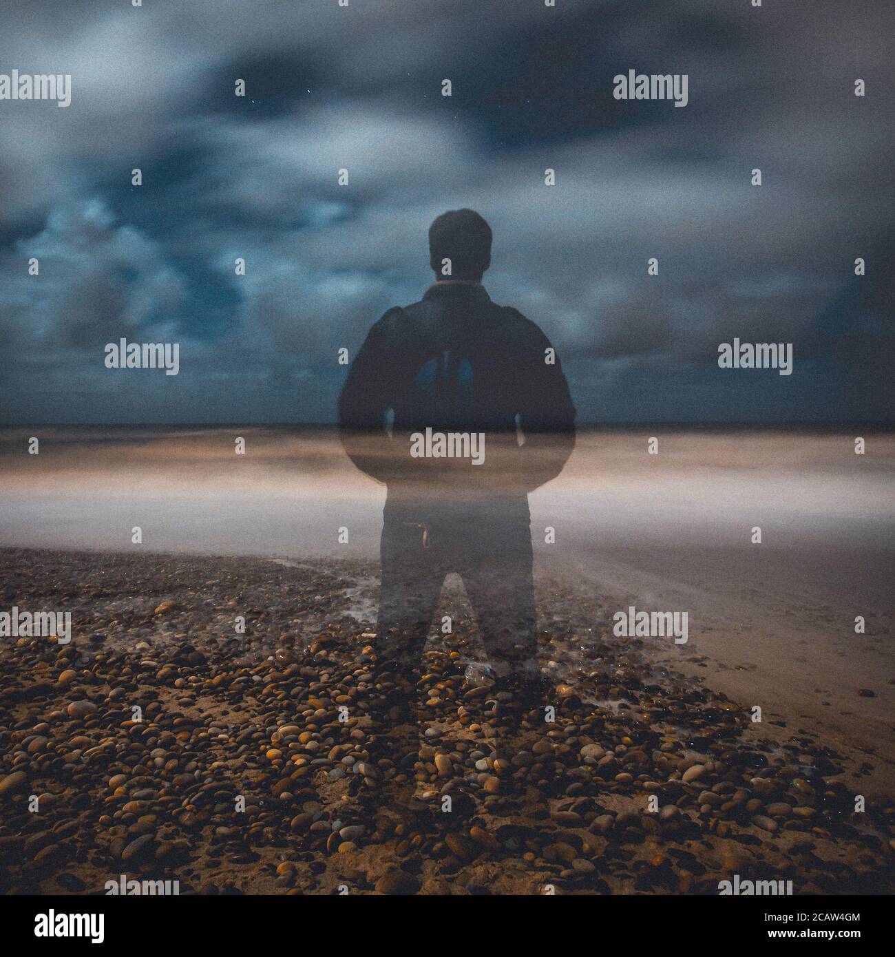 Blurry person standing on the pebbles at the beach under the cloudy sky ...