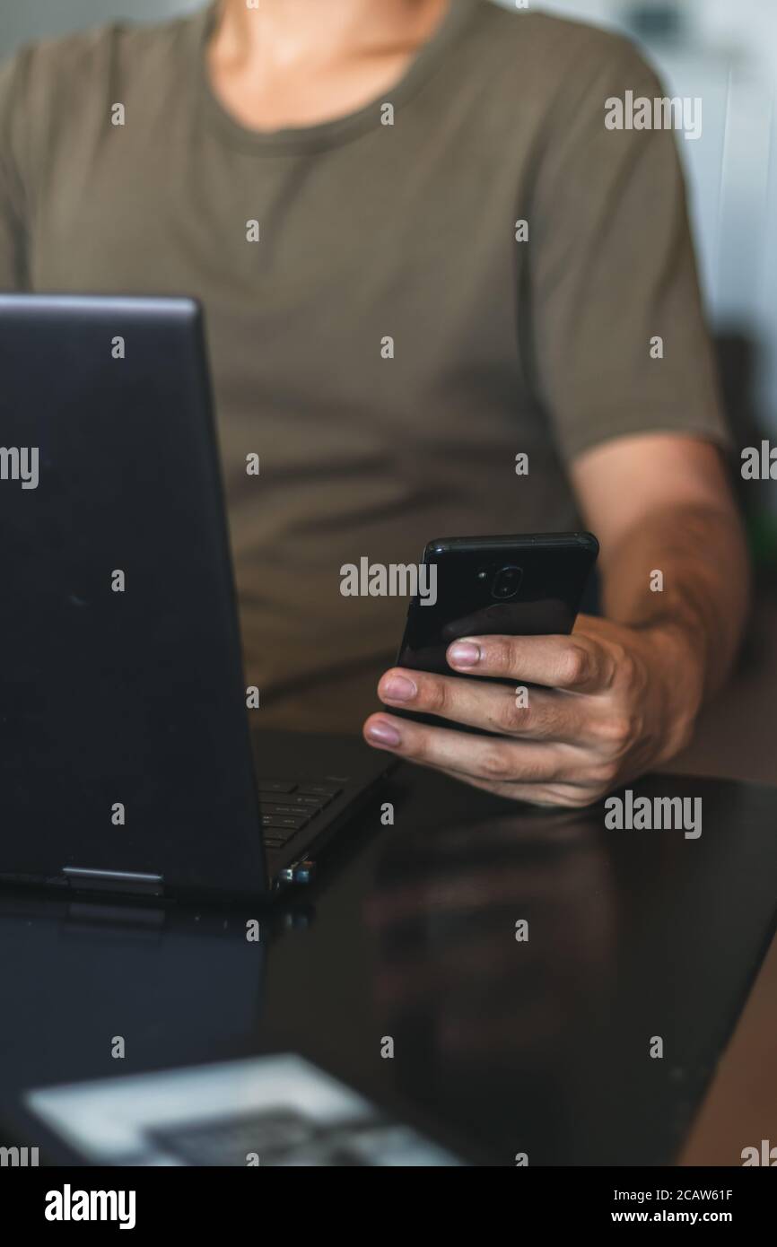 Vertical shot of male hands using a laptop and cellular ohone Stock ...