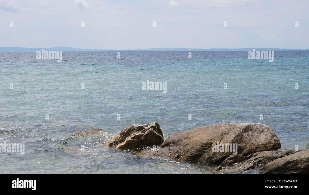 Wavy ocean hitting the rocks and gleaming under the blue sky Stock ...