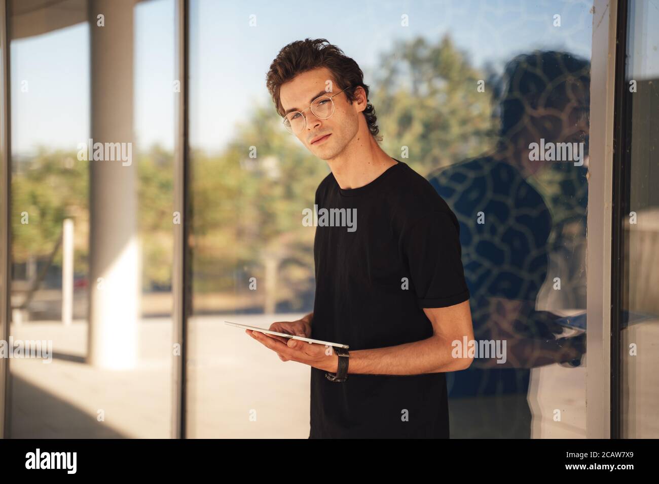 Portrait of confident young man holding tablet computer while standing ...