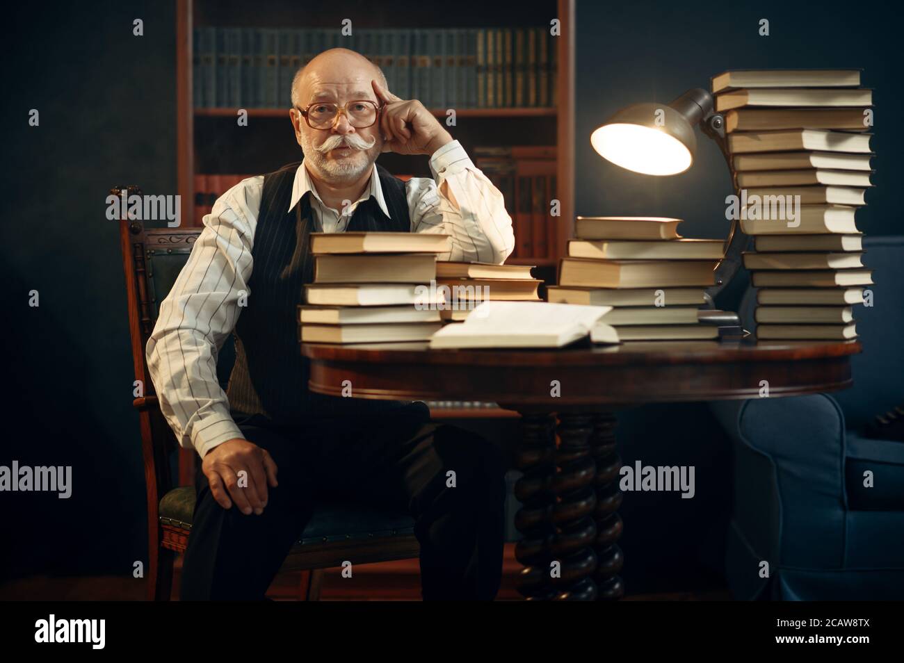 Elderly writer sitting at the table with books Stock Photo - Alamy
