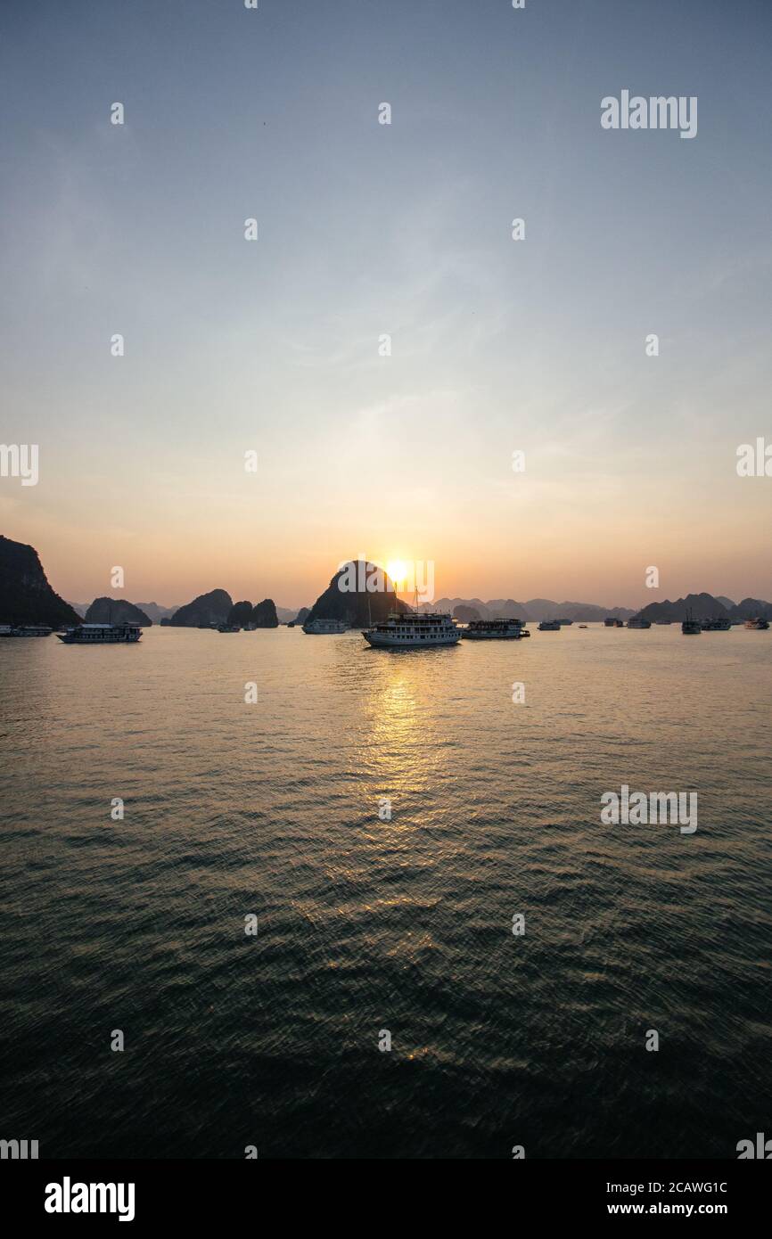 Tourist boats cruising through Ha Long with a beautiful sunset sky in ...