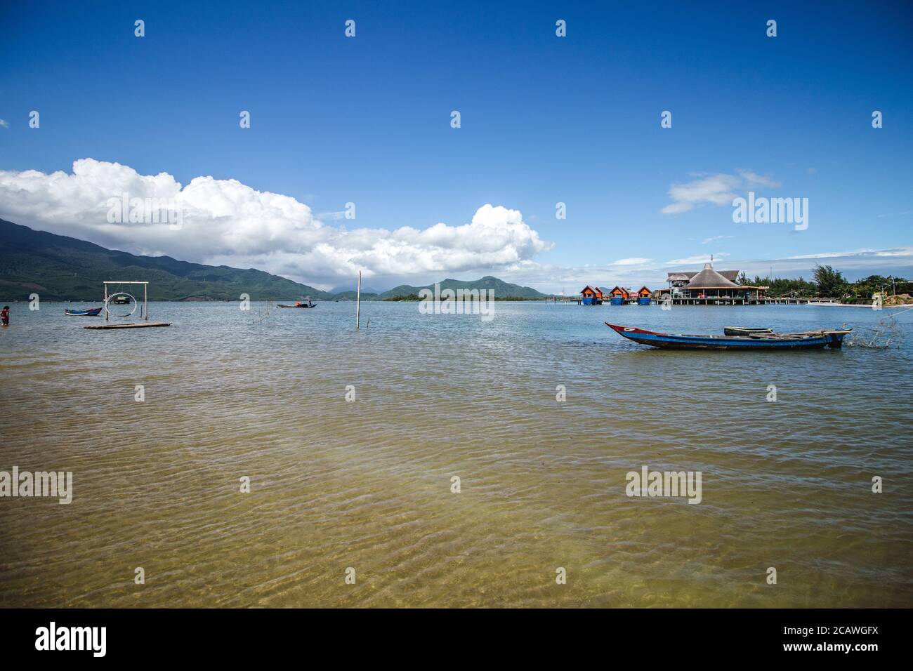 Lake resort at Lang Co in Vietnam with boats and huts under a blue sky ...