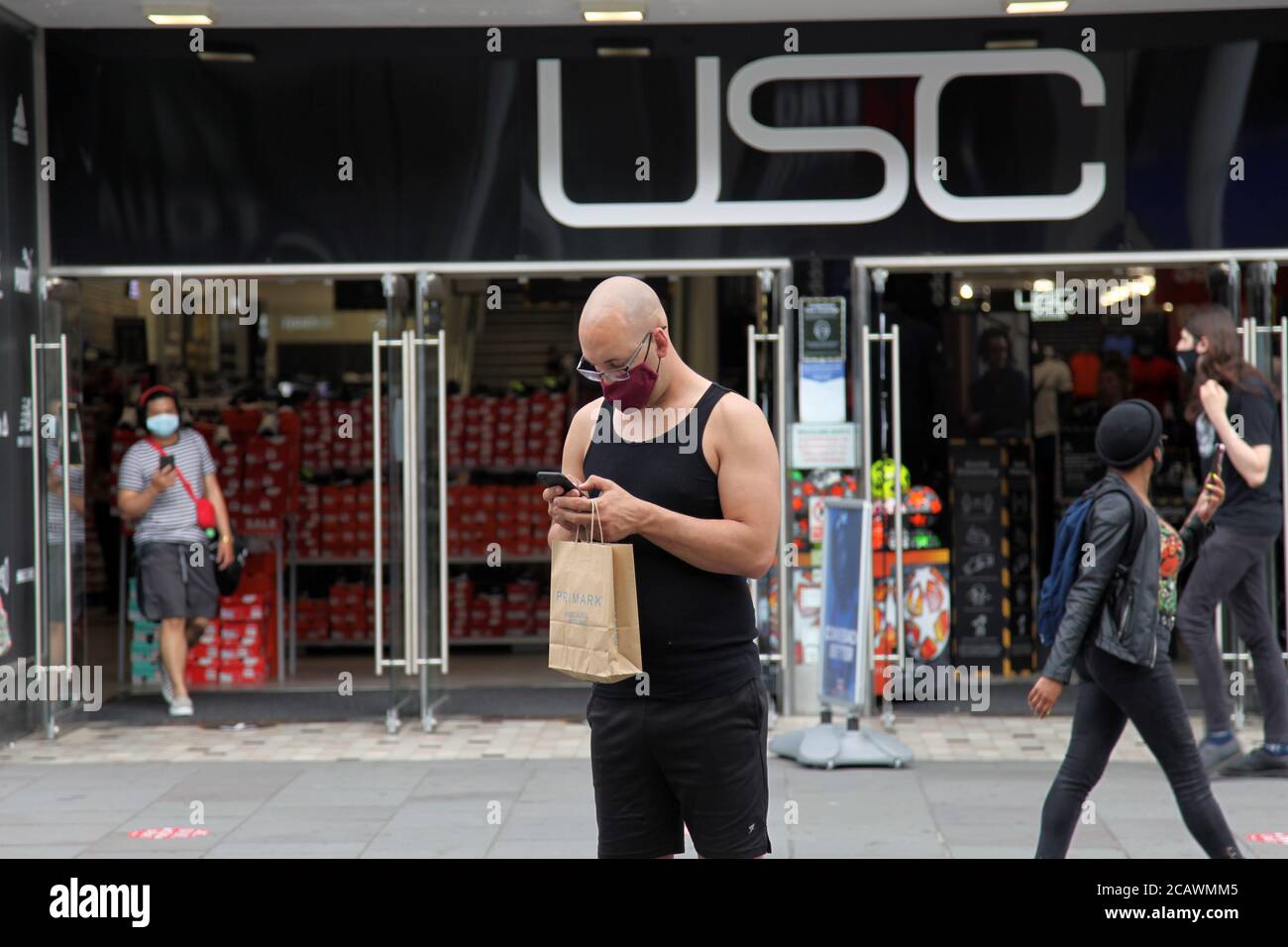 A bald man sends a text message whilst wearing a facemask PPE outside ...