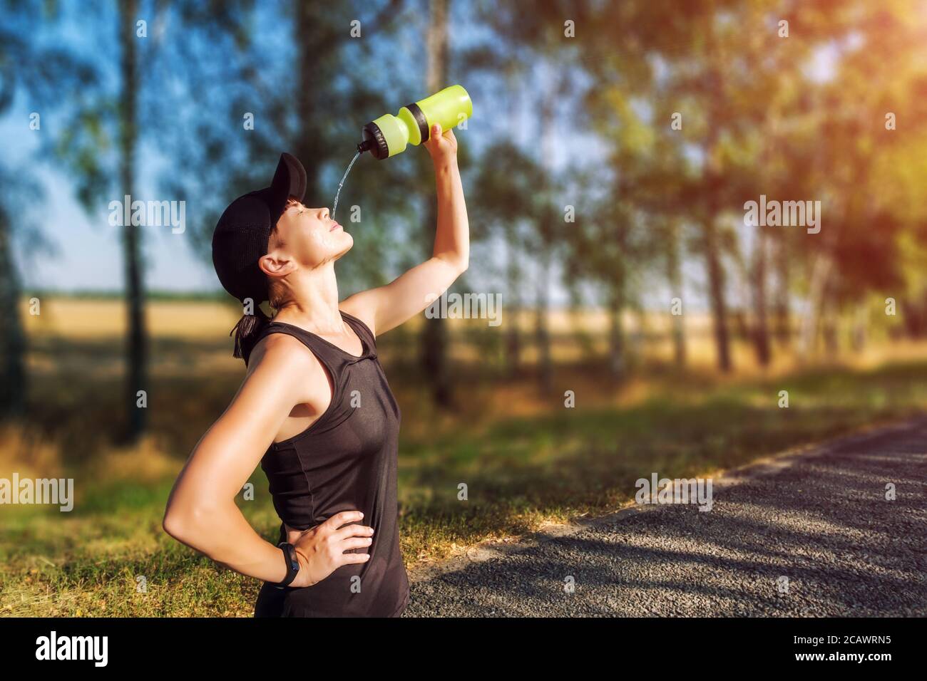 Resting young woman pouring water from bottle on her face after hard ...