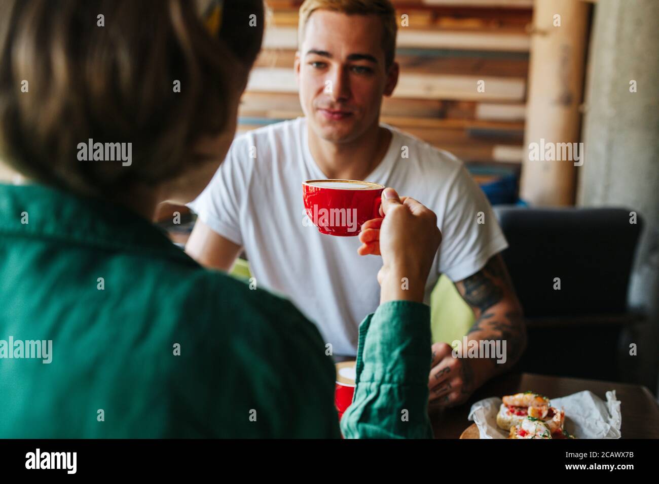 Two people on a date in a cafe sitting in front of each other, drinking ...
