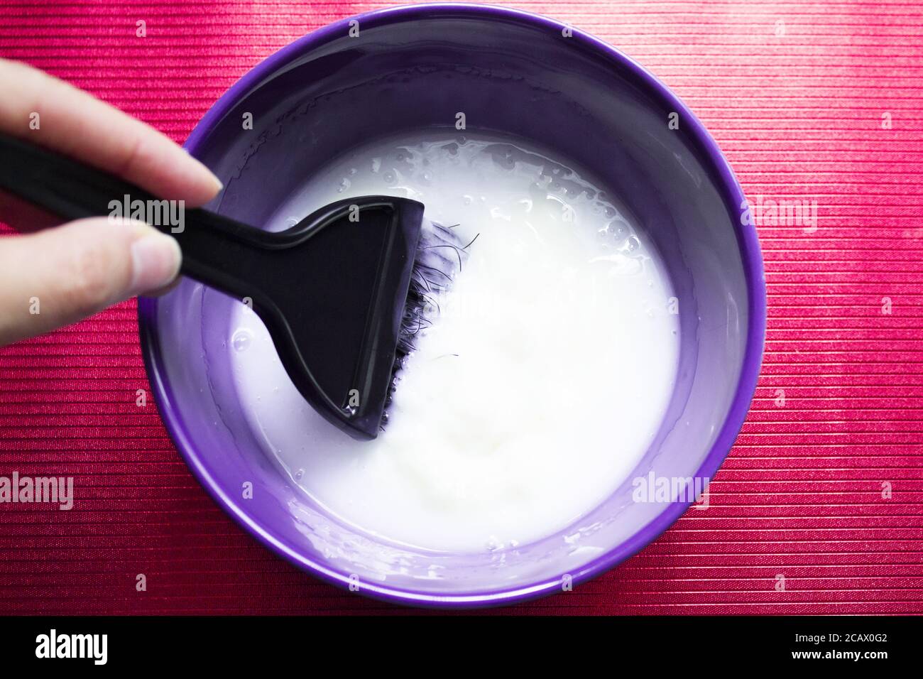 Blue bowl with mix to dye hair. Womans hand removing the dye mixture ...