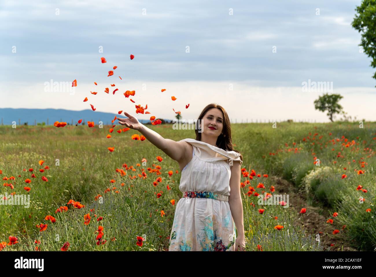 Young woman in a white dress throwing red poppy flowers at the camera ...